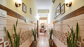 Corredor de hotel com azulejos estampados, plantas em vasos e quadros nas paredes.