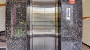 Um elevador com interior em aço inoxidável, um aviso de proibido fumar e uma placa indicativa da localização do elevador.