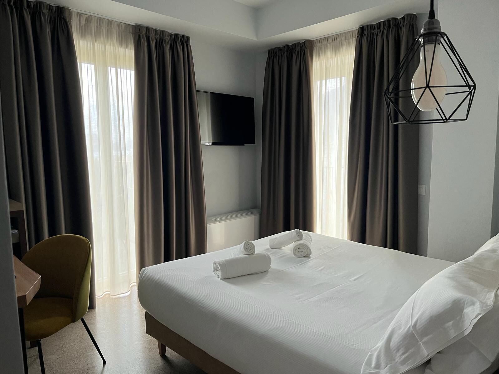 Quarto de hotel com cama, televisão na parede e uma cadeira.