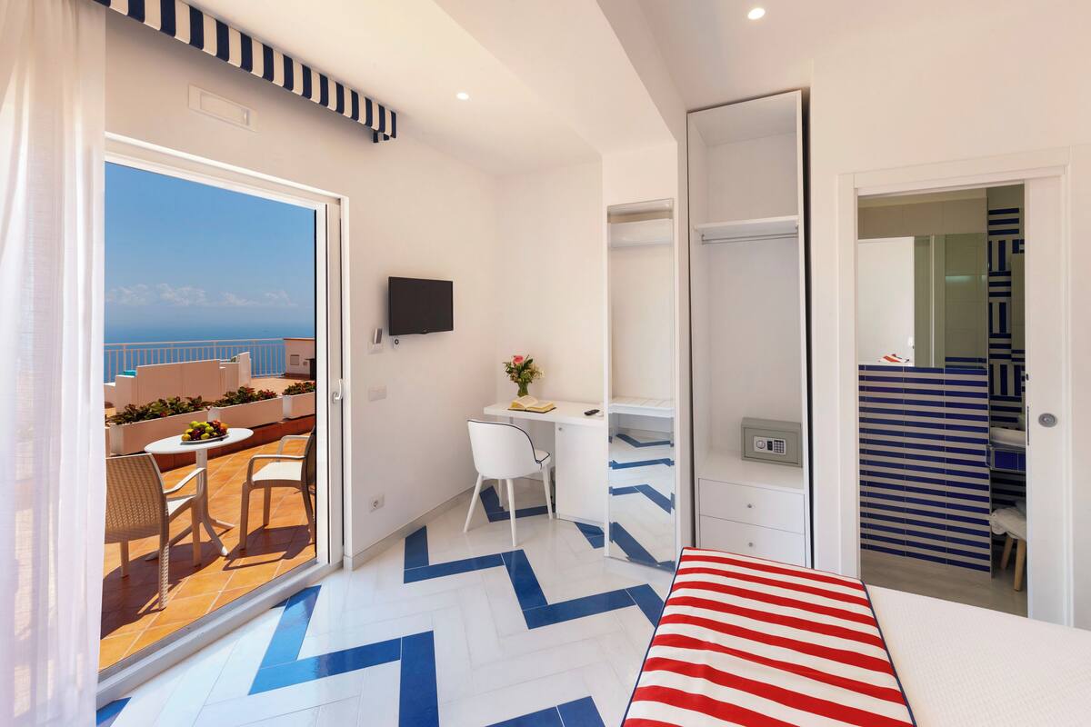 Quarto de hotel moderno com varanda, escrivaninha, cadeira e cama.