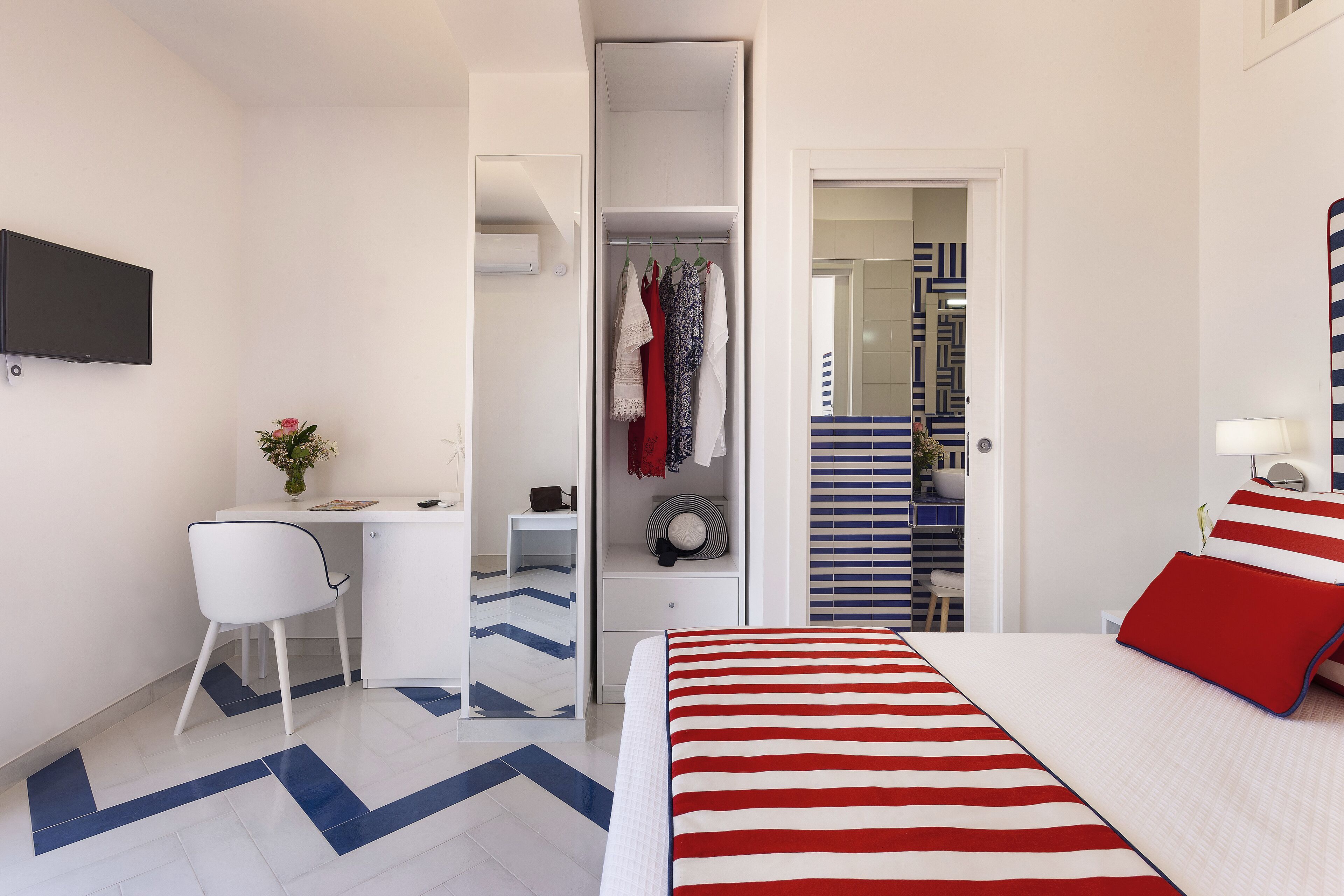 Quarto de hotel com cama, escrivaninha, cadeira, guarda-roupa e televisão.