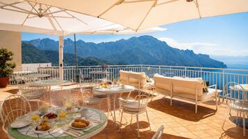 Terraço com área de estar externa, mesa com café da manhã e vista para as montanhas.