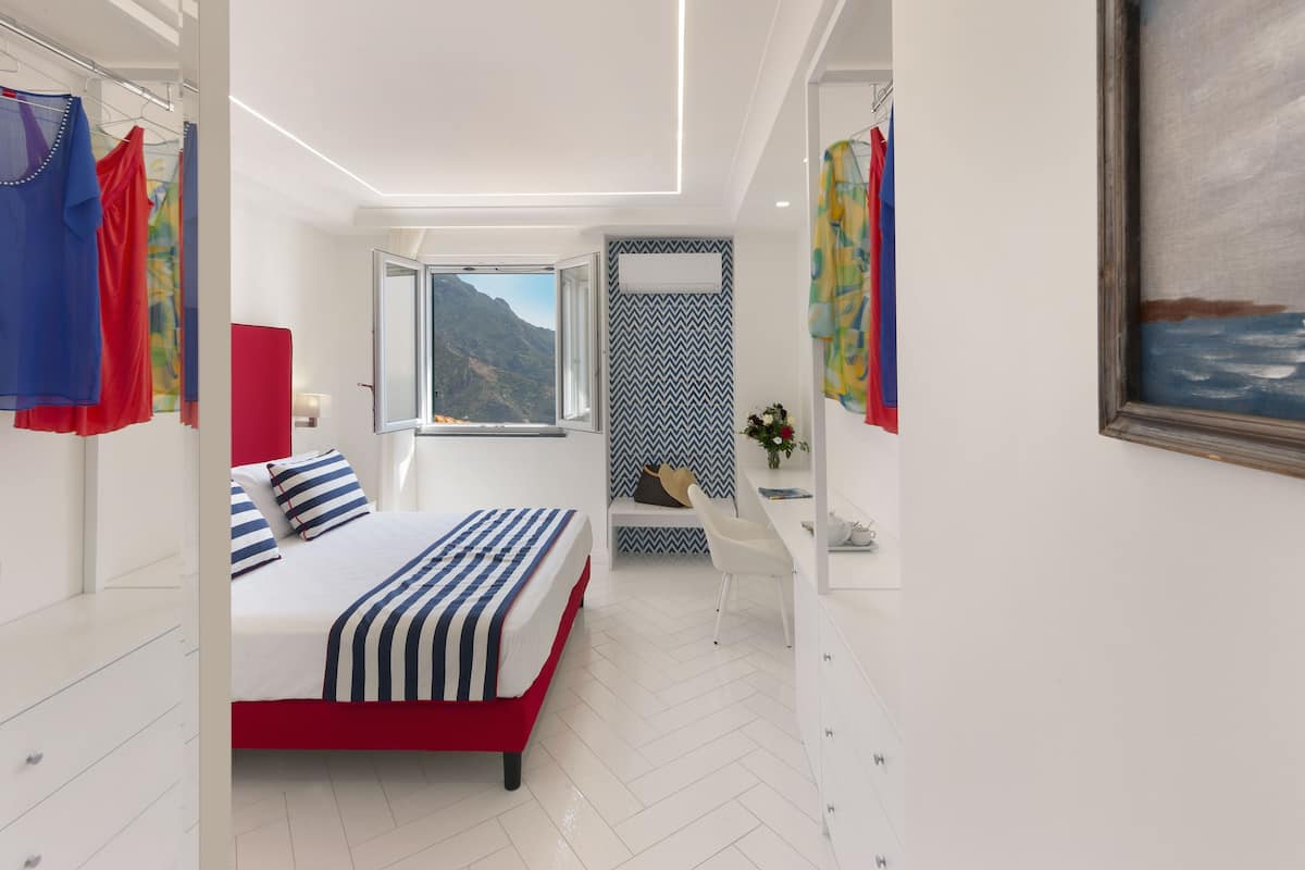Quarto moderno com cama, escrivaninha e vista para montanhas.