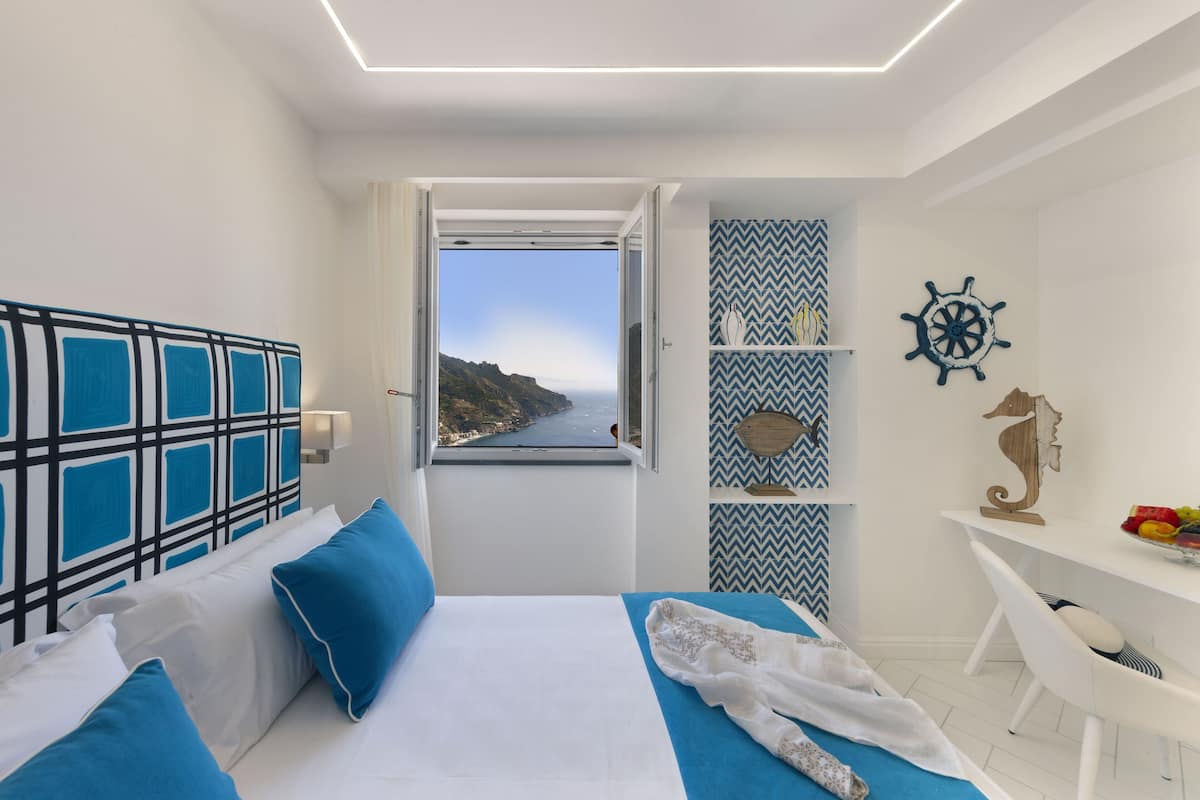 Quarto com cama, escrivaninha e vista para o mar.