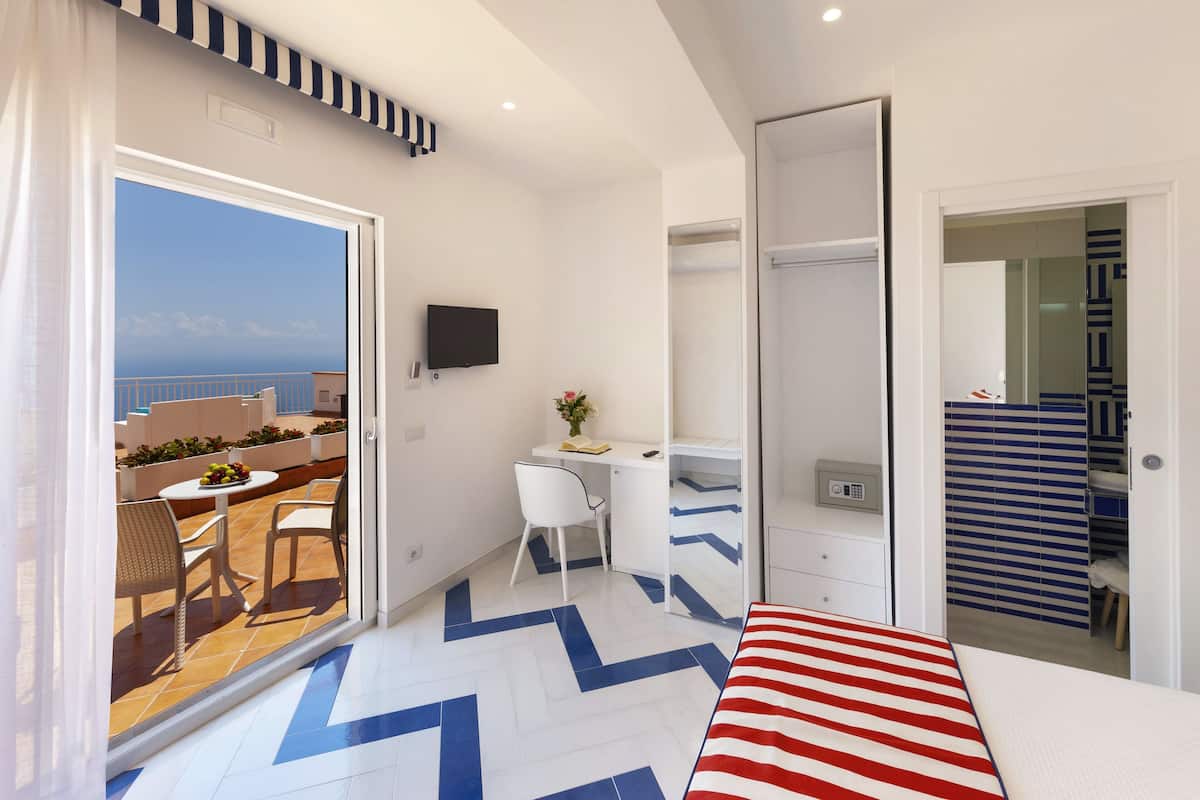 Quarto de hotel moderno com varanda, escrivaninha, cadeira, cama e guarda-roupa.
