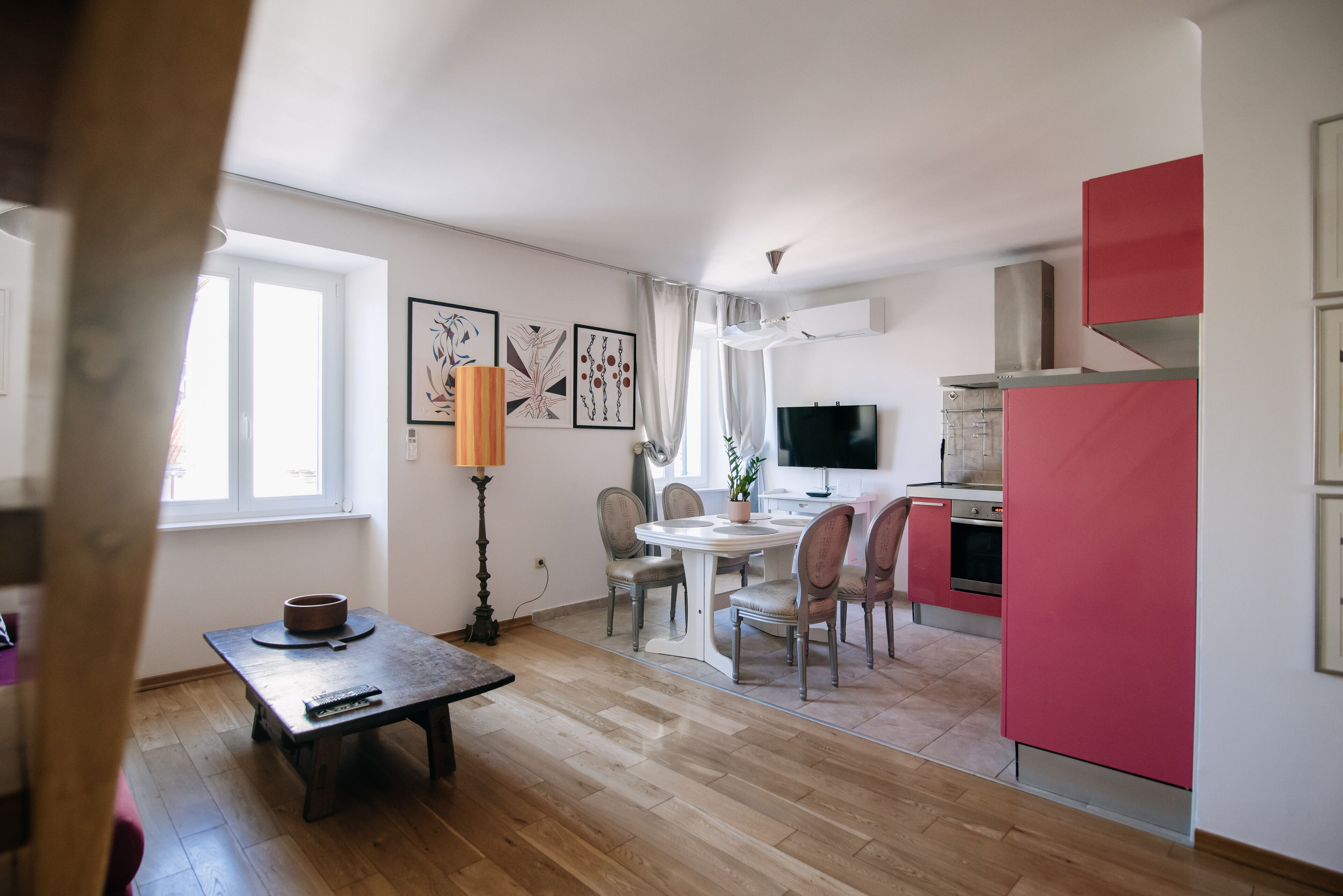 Uma sala de estar moderna com área de jantar, uma cozinha com armários vermelhos e uma televisão.