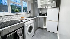 Uma cozinha compacta com máquina de lavar, pia e bancada com torradeira e cafeteira.