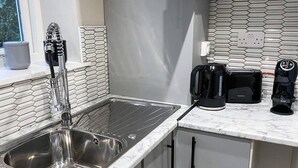 Uma cozinha com uma pia de aço inoxidável, uma cafeteira e uma torradeira na bancada.