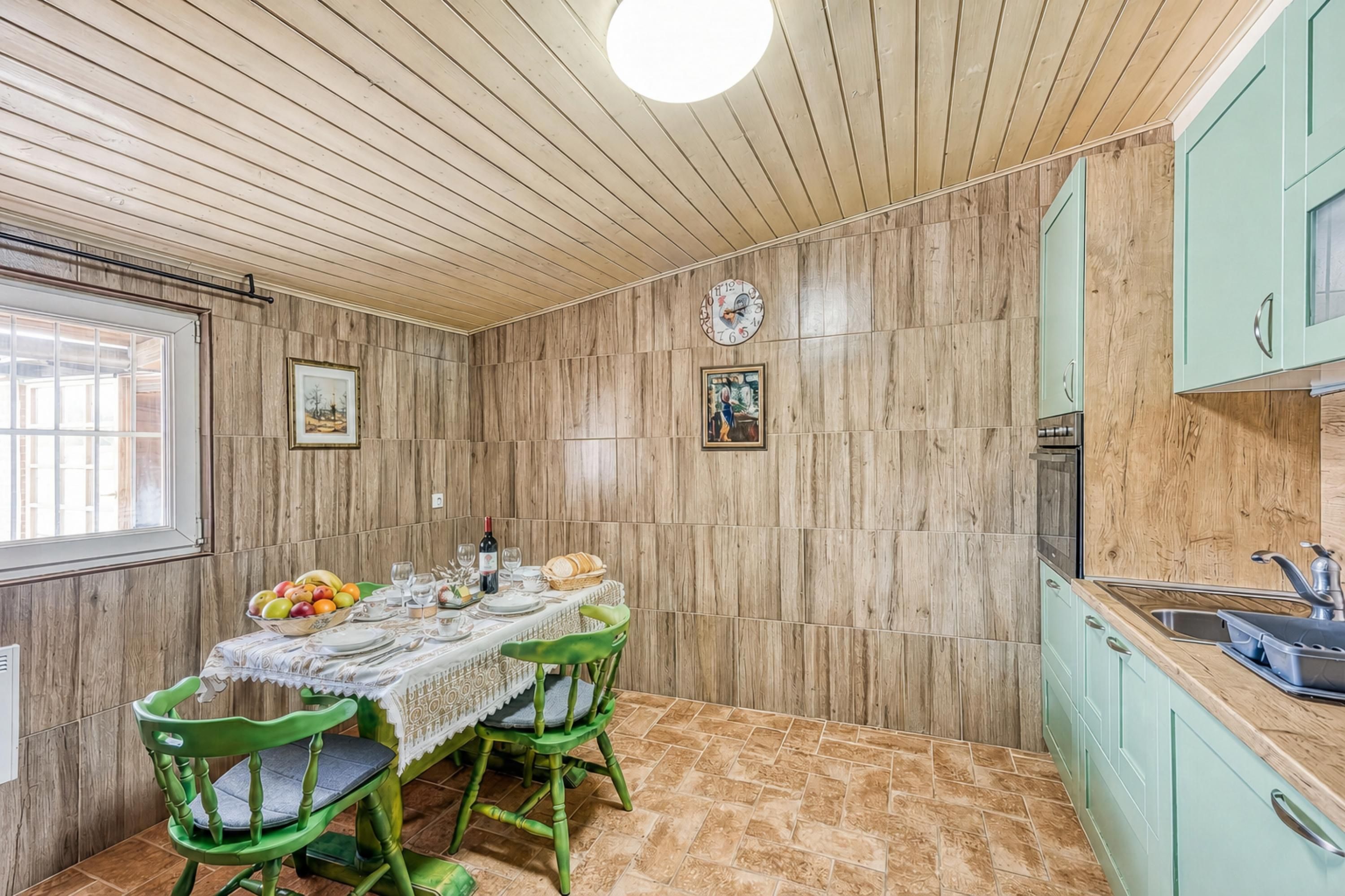 Uma área de refeições com uma mesa posta para dois, um relógio na parede e uma janela com persianas.