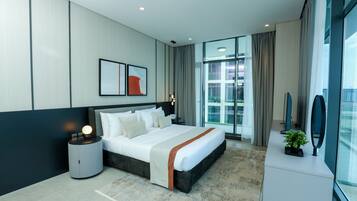 Quarto de hotel moderno com uma cama grande, mesa de cabeceira com abajur, televisão e vista da cidade através de janelas amplas.