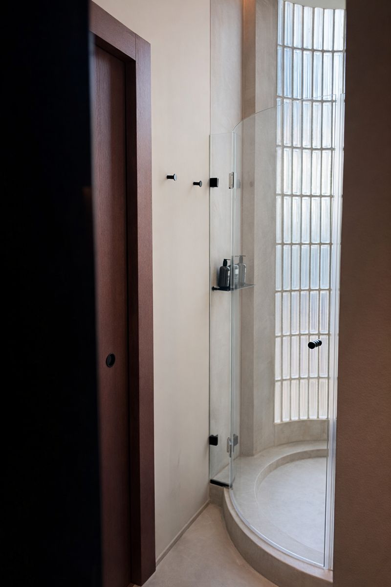 Casa de banho de canto com cabine de duche em vidro, porta e janela com persianas verticais.