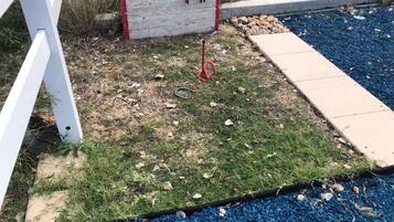 Uma área de jardim com uma estrutura de metal branca, um banco pintado em vermelho e branco e um tapete de borracha azul.