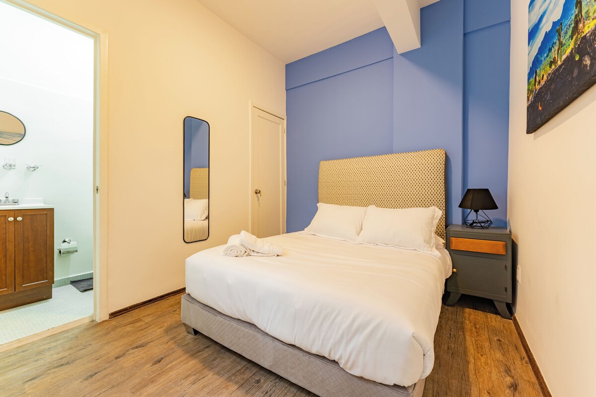 Quarto com cama grande, mesa de cabeceira, espelho e quadro na parede.