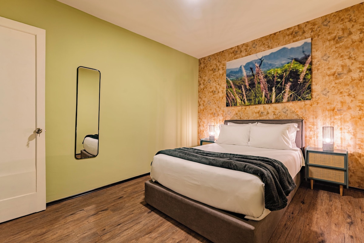 Quarto com cama, mesa de cabeceira, espelho e quadro na parede.