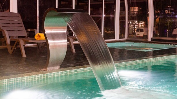Piscina com cascata, área de estar com cadeiras e vista para o exterior.