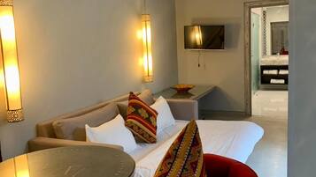 Quarto de hotel moderno com cama, uma cadeira vermelha, uma mesinha e uma TV.