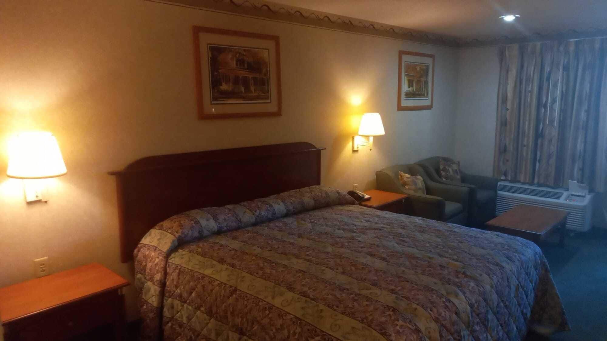 Quarto de hotel com uma cama grande, duas luminárias de cabeceira, uma mesinha, um sofá e um ar condicionado.