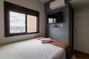 Quarto com cama, janela, televisão na parede e aparelho de ar condicionado.