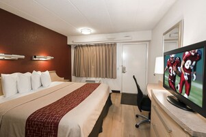 Quarto de hotel com cama, televisão, escrivaninha e uma cadeira.
