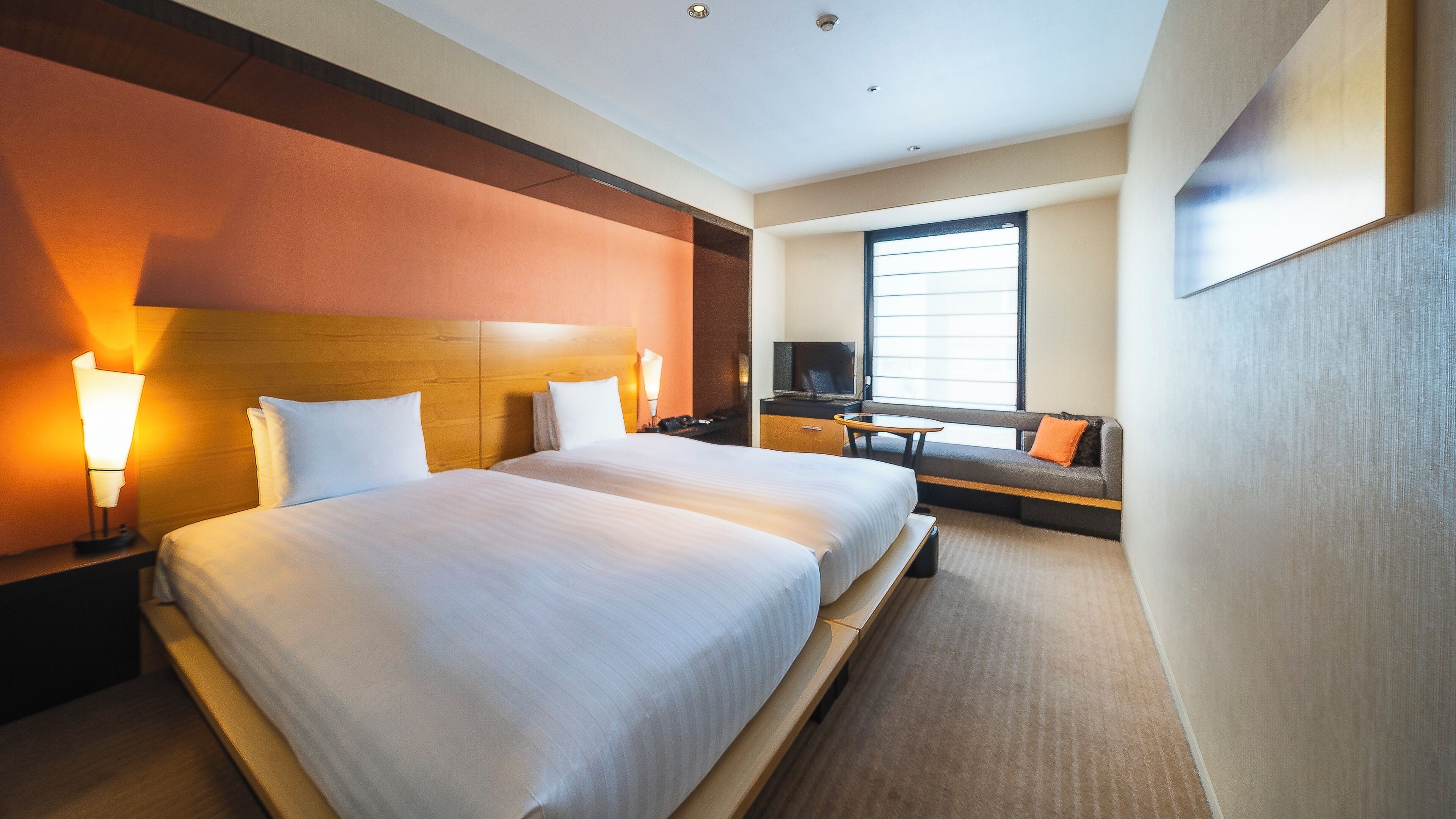 Quarto de hotel com uma cama grande, luminárias de cabeceira, televisão, sofá e uma janela.