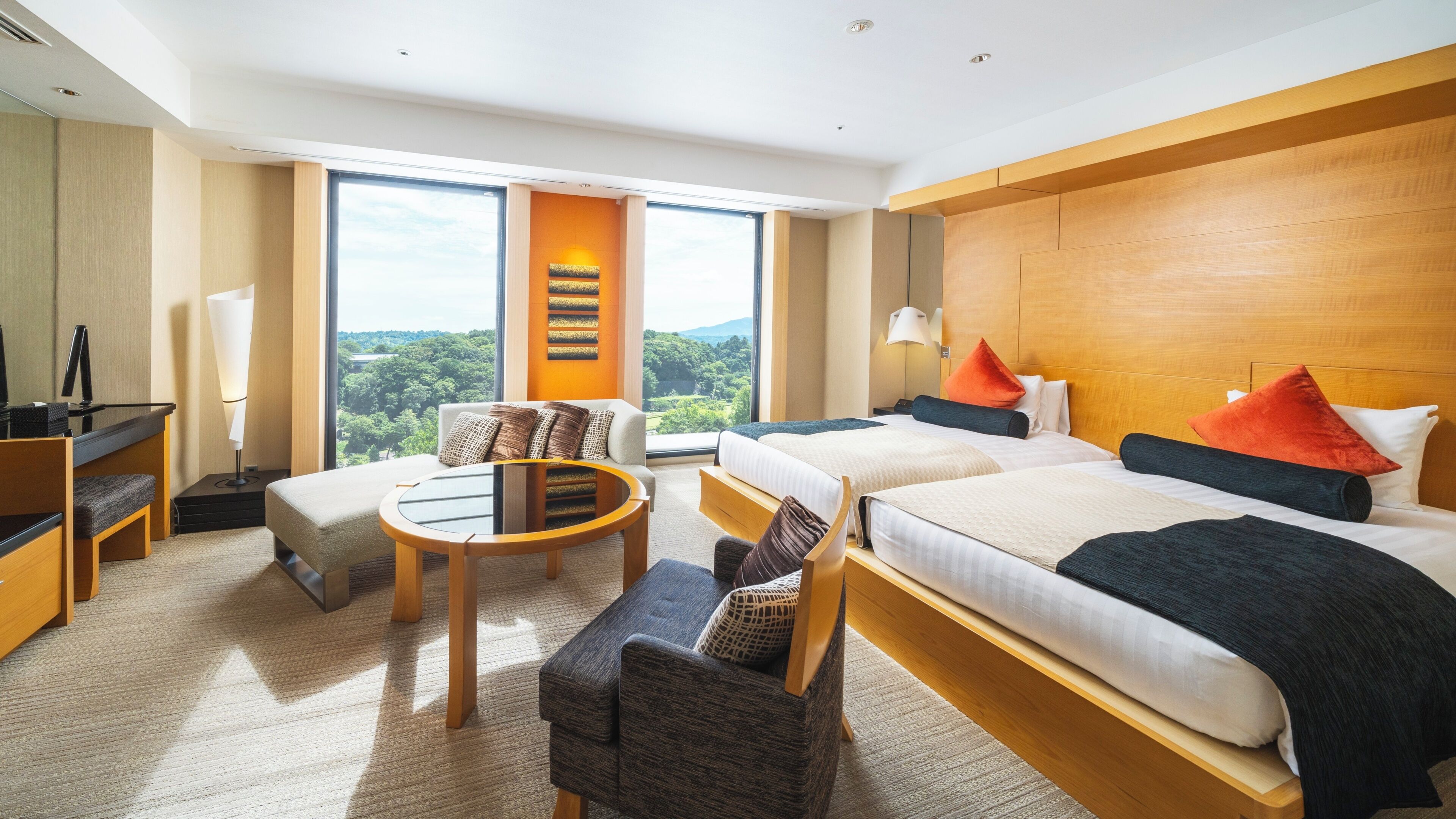 Quarto de hotel com cama, escrivaninha, cadeira, mesinha e vista para o exterior.