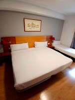 Quarto de hotel com uma cama grande, uma mesinha de cabeceira, um criado-mudo e uma luminária fixada na parede.