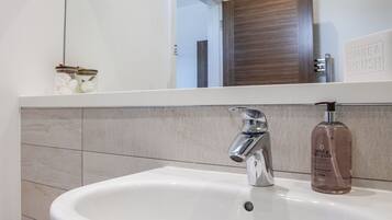 Casa de banho com lavatório branco, torneira cromada e frasco de sabonete líquido.