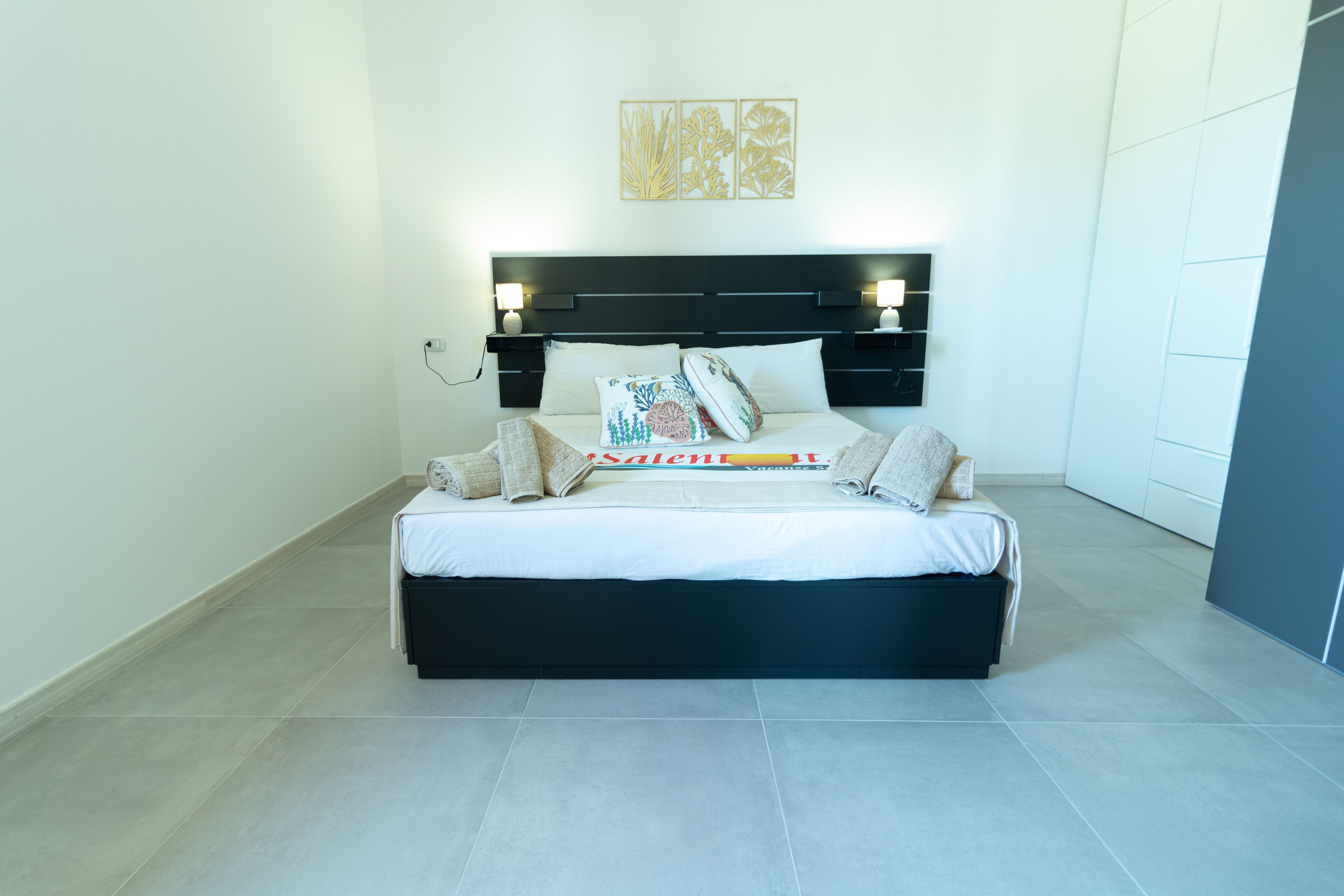 Quarto moderno com cabeceira preta, roupa de cama branca e almofadas decorativas.
