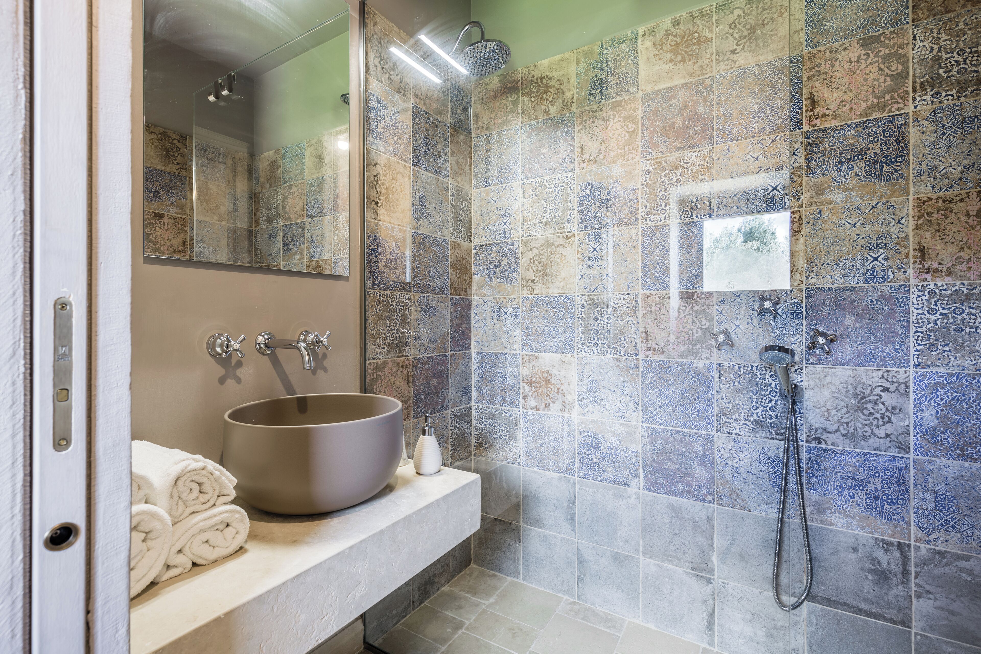 Casa de banho com uma pia grande, espelho e área de duche com azulejos estampados.