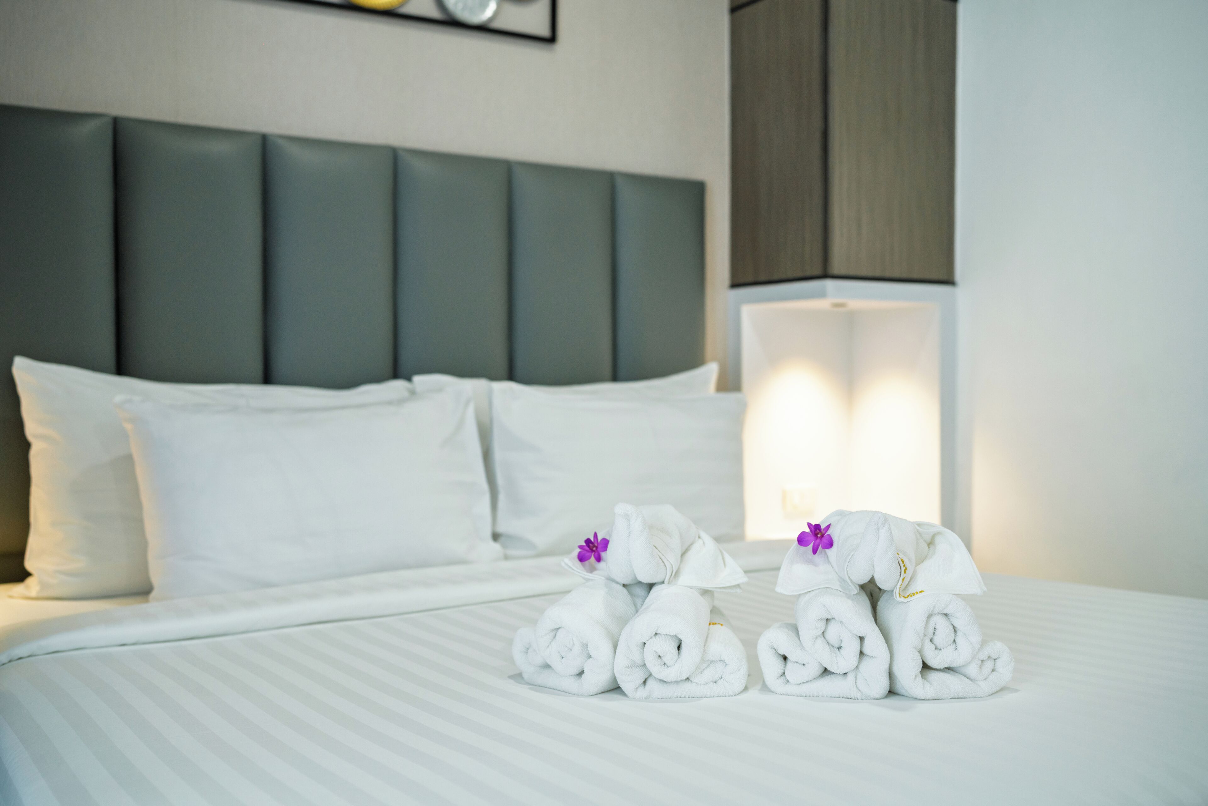 Quarto de hotel com cama, almofadas, cabeceira e toalhas dispostas sobre a cama.