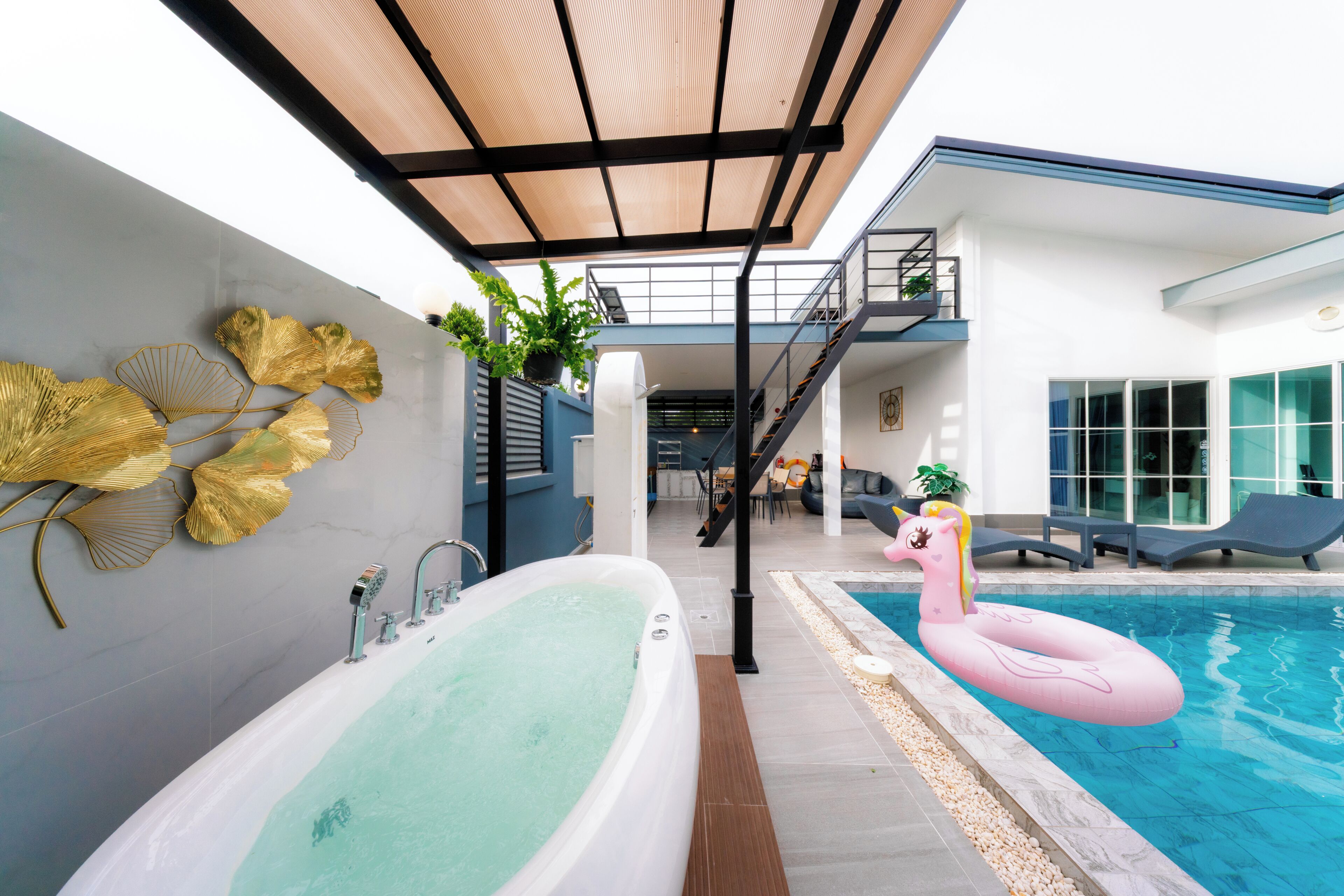 Uma área interna de piscina moderna com uma banheira grande, um flutuador de unicórnio rosa e uma escadaria que leva a um nível superior.