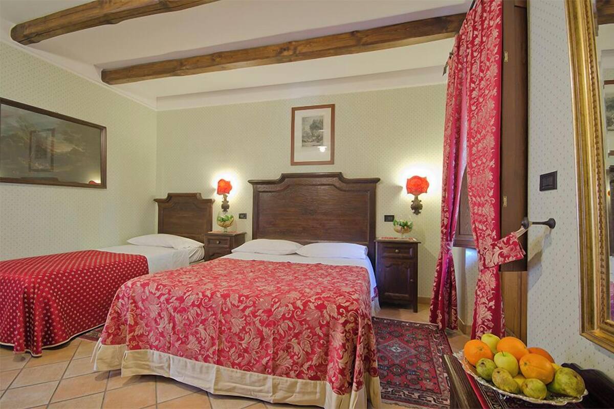 Quarto com duas camas, vigas de madeira no teto, um quadro na parede e uma cesta de frutas no chão.
