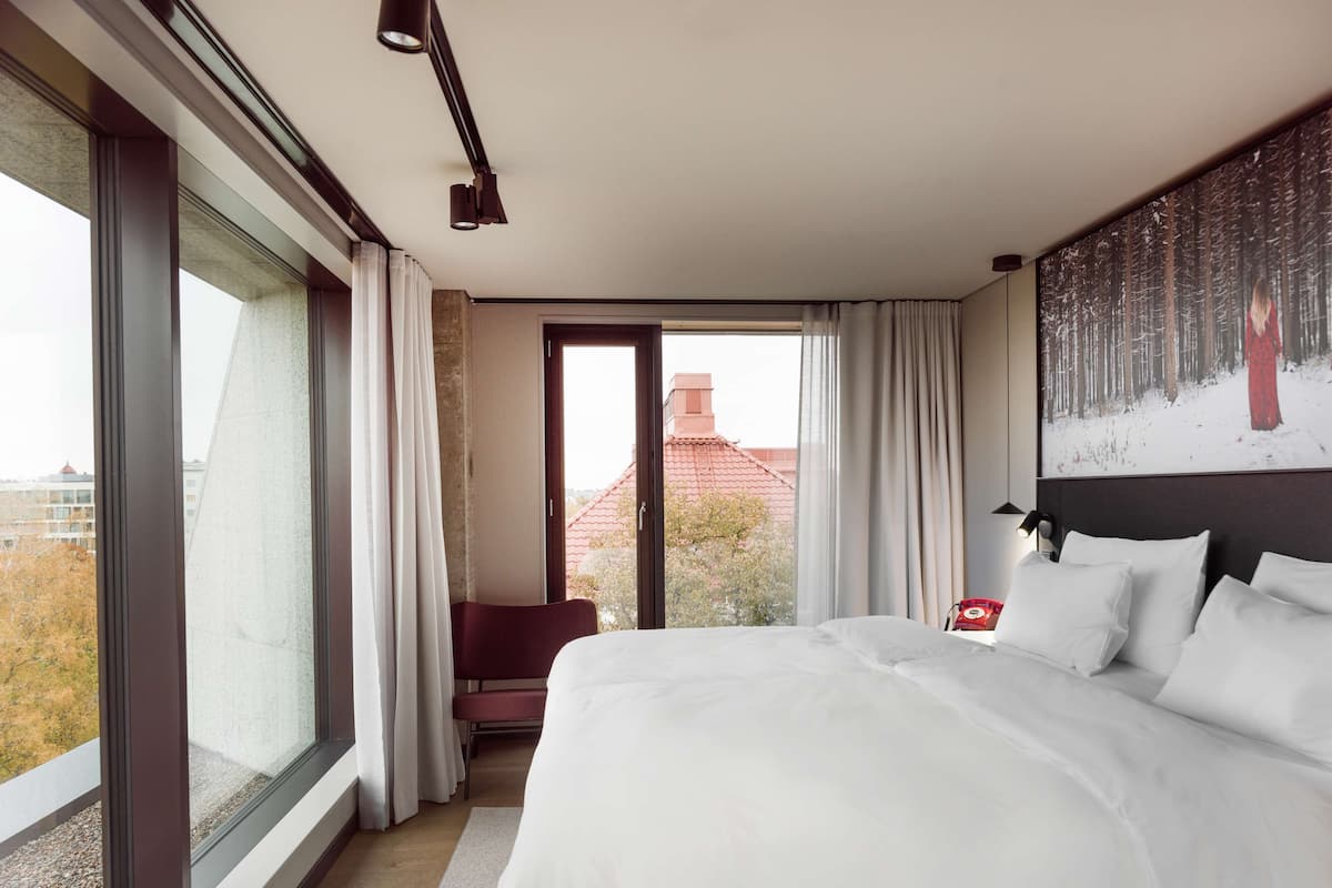 Quarto de hotel moderno com uma cama grande, uma escrivaninha e vista para a cidade.
