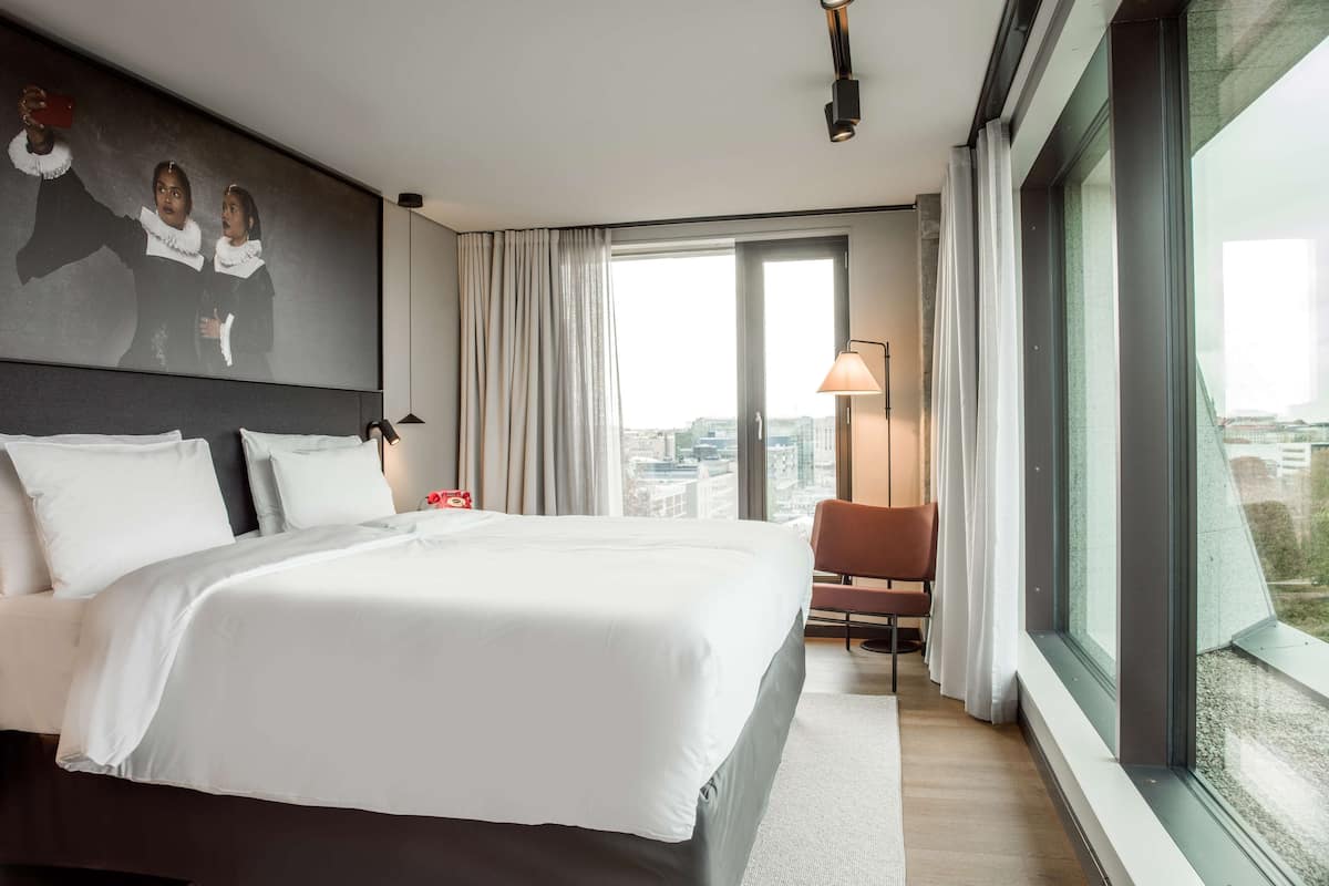 Quarto de hotel moderno com uma cama grande, vista para a cidade e decoração minimalista.