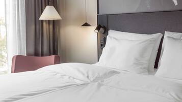 Quarto de hotel com cama, cadeira, luminária e janela com cortinas.