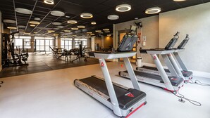 Academia com esteiras, aparelhos de musculação e uma grande janela que proporciona iluminação natural.
