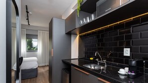 Cozinha moderna com bancadas pretas, pia e máquina de café. Há uma janela com cortinas e vista para o verde lá fora.