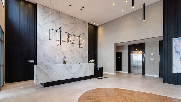 Uma área de recepção moderna com um balcão de mármore, piso de madeira e luminária geométrica.