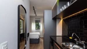 Quarto de hotel compacto com cozinha compacta, uma cama, espelho e vista para o exterior.