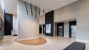 Um hall amplo com piso de madeira curvado, um banco preto e um grande quadro abstrato na parede.
