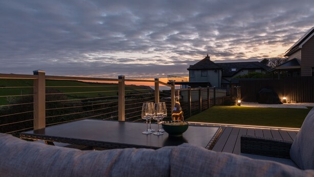 Terraço com mesa, três copos de vinho e um recipiente com petiscos.