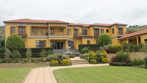 Uma casa amarela de vários andares com telhado em tijolos, porta de entrada e um pequeno jardim com um caminho que leva à entrada.