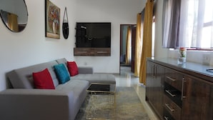 Uma sala de estar moderna com um sofá seccional cinza, uma mesinha de centro e uma área de cozinha com armários de madeira e bancada.