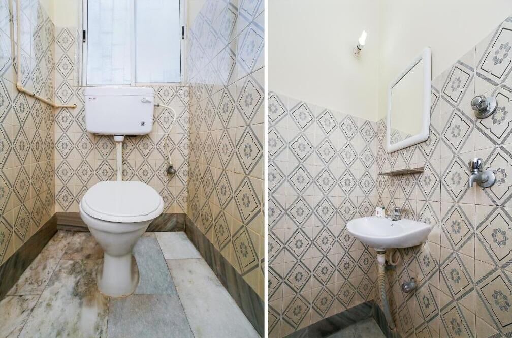 Casa de banho com sanita e lavatório, paredes em azulejo, janela e espelho.