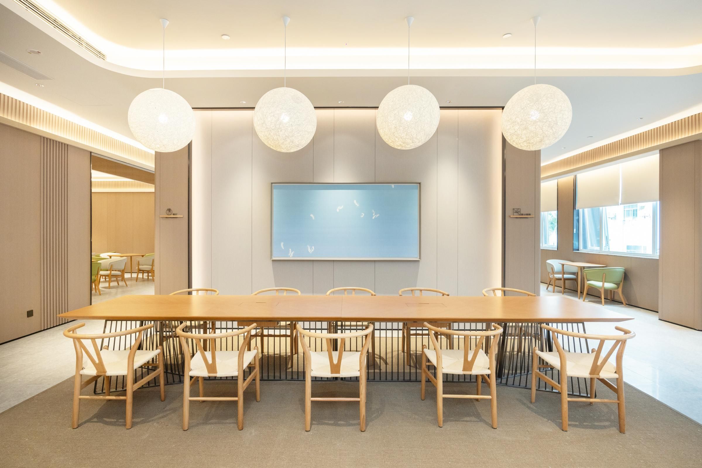 Uma sala de conferências com uma mesa comprida, seis cadeiras e três grandes luminárias pendentes esféricas.