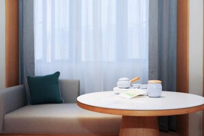 Quarto moderno com mesa de madeira redonda, sofá e janela com cortinas leves.