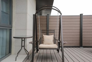 Um deck de madeira com uma cadeira de balanço e uma mesa pequena.