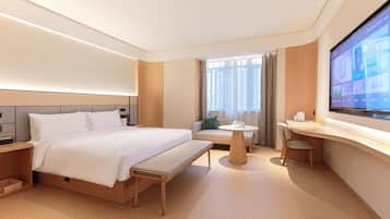Quarto de hotel moderno com uma cama grande, uma escrivaninha, um sofá e uma televisão na parede.