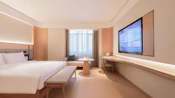 Quarto de hotel com uma cama grande, uma escrivaninha, uma cadeira e uma televisão fixada na parede.