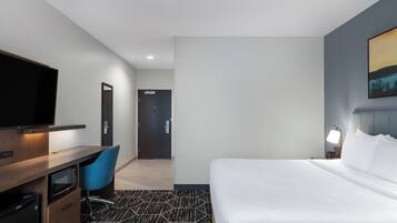 Quarto de hotel com cama, escrivaninha com computador, televisão e porta para outro cômodo.